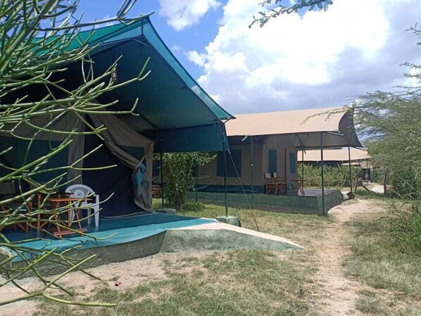 Uma área externa com tendas, uma mesa, cadeiras, um espaço de estar coberto e um edifício ao fundo.