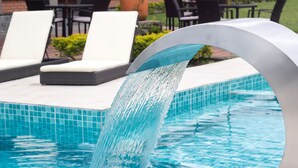 Piscina com um elemento aquático, espreguiçadeiras e área de estar externa.