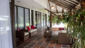 Uma ampla área de varanda com móveis de vime, janelas grandes e teto com vigas de madeira.