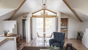 Um amplo loft com teto alto, área de jantar com mesa e cadeiras redondas, cozinha com armários de madeira e uma grande janela com vista para o exterior.