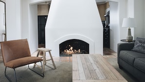 Uma sala de estar com lareira, um sofá, uma mesa de centro e uma poltrona.