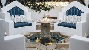 Uma área externa moderna com espaço para sentar, uma lareira central e uma fonte decorativa.
