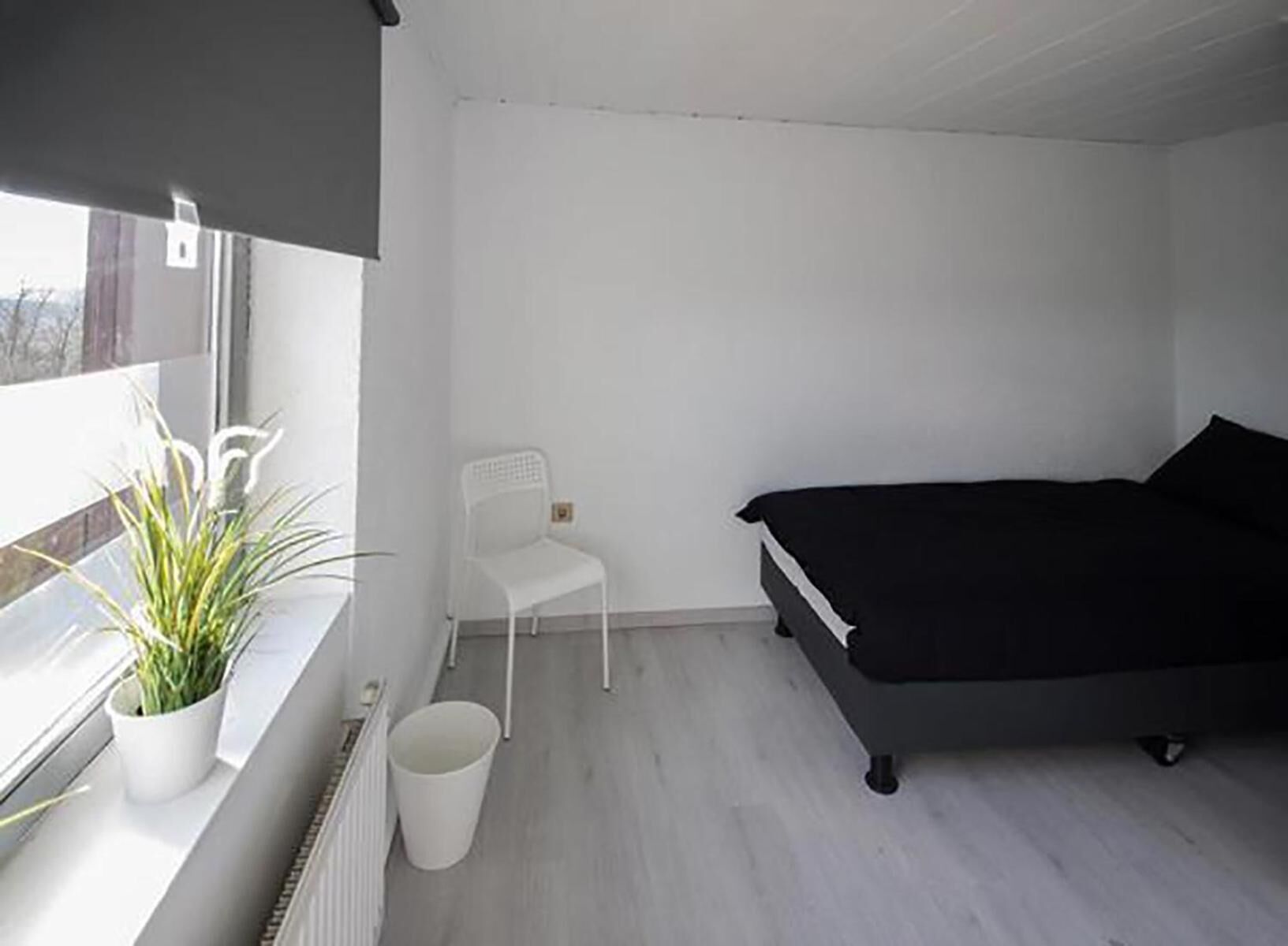 Quarto moderno com uma cama, uma cadeira, um vaso de planta e um radiador.
