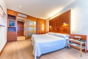 Quarto de hotel com uma cama grande, guarda-roupa de madeira e uma mesa com telefone e papéis.