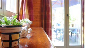 Uma mesa de madeira com plantas em vasos e vista para área externa através de uma porta de vidro.