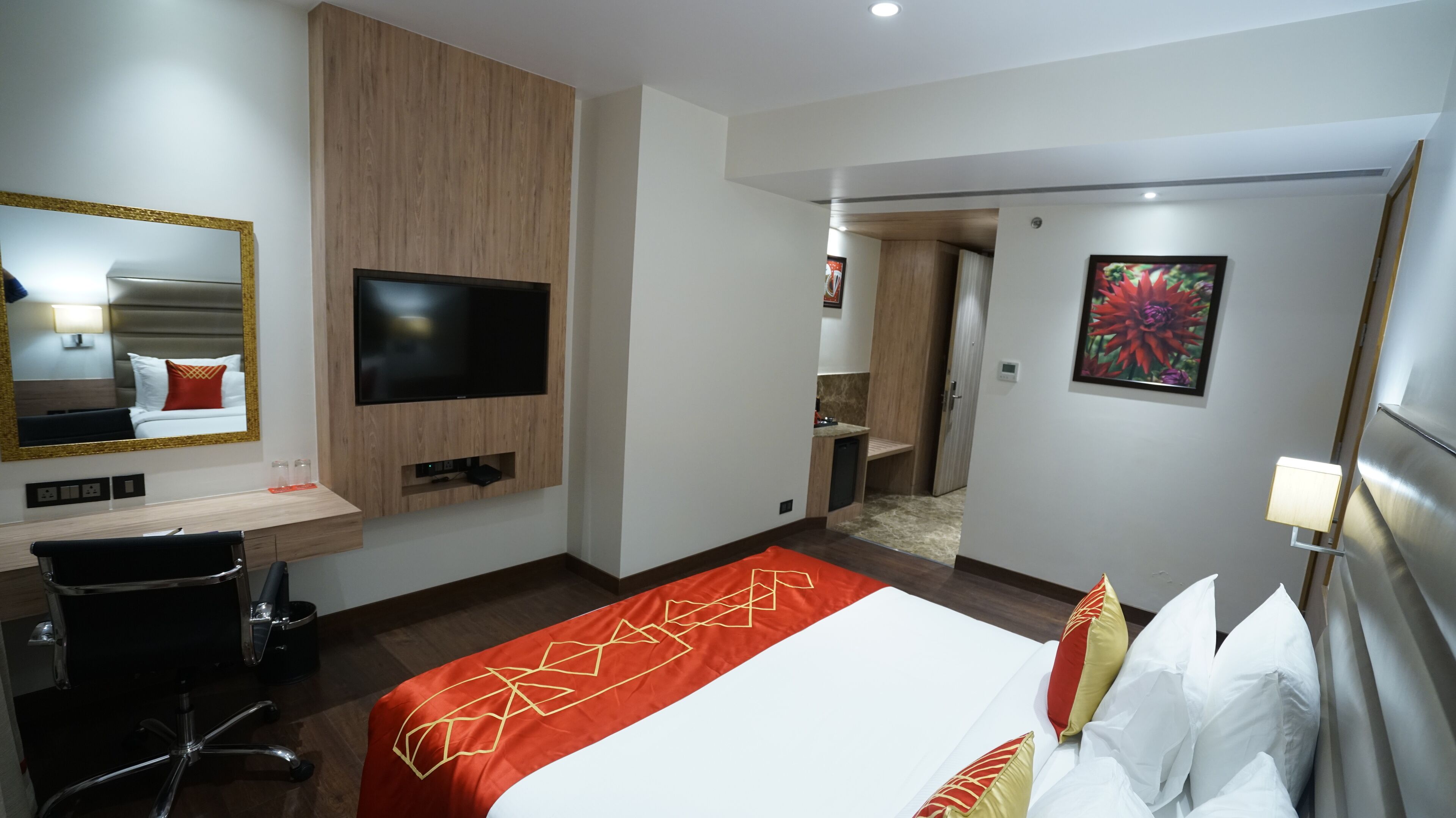 Quarto de hotel com uma cama grande, televisão na parede, secretária com cadeira e banheiro visível por uma porta aberta.