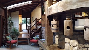 Um interior acolhedor com lareira de pedra, mobiliário de madeira e escada que leva a um andar superior.