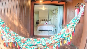 Uma rede em um deck de madeira, com vista para um quarto através de uma porta de vidro.