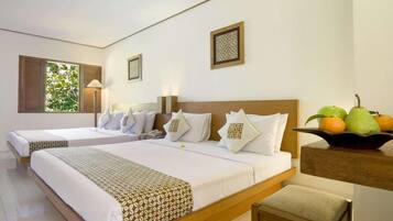 Quarto de hotel com duas camas, uma escrivaninha com frutas e janela com vista para o verde.