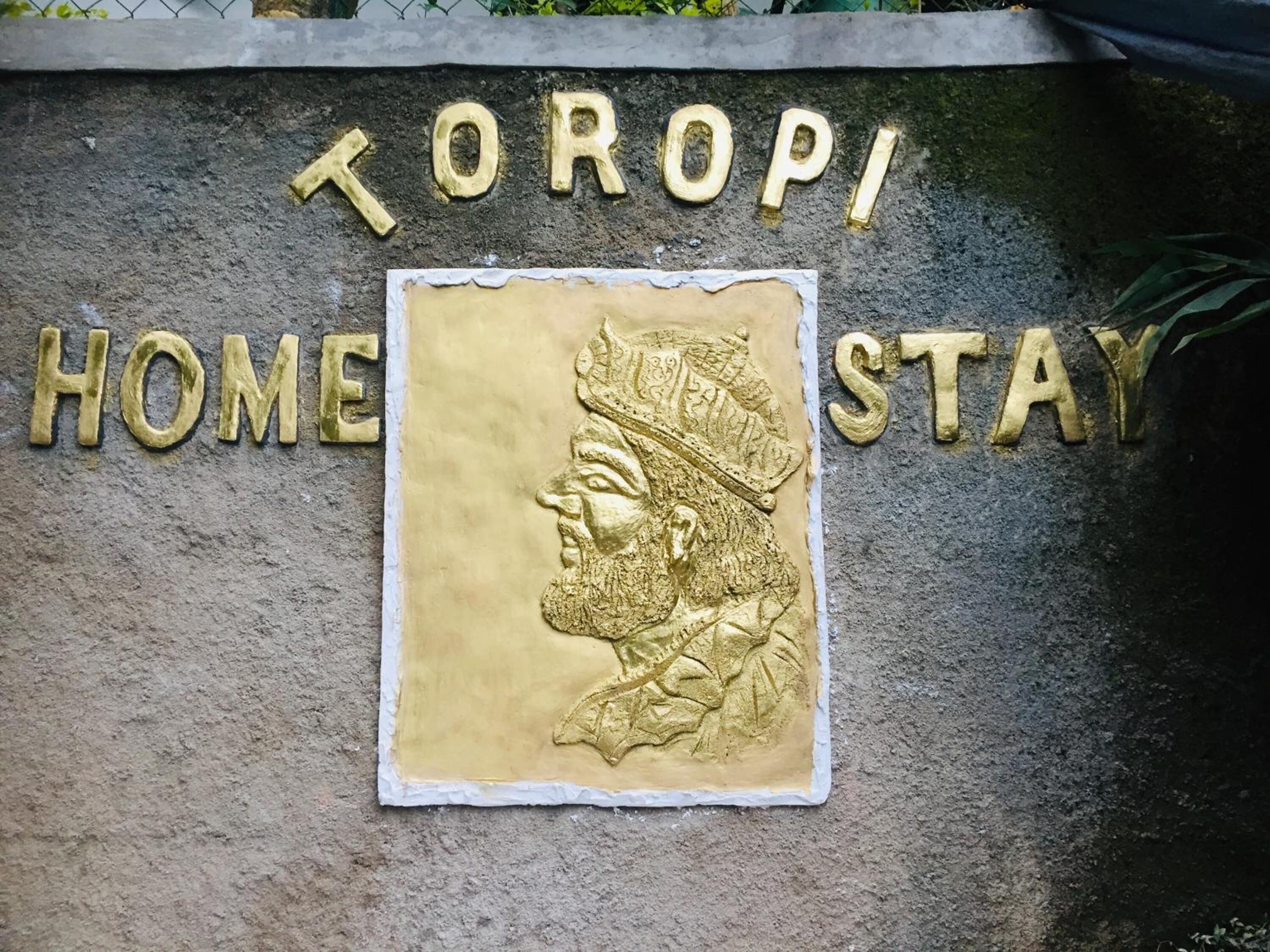 Placa com os dizeres 'TOROPI HOME STAY' e um relevo dourado do perfil de uma pessoa.