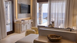 Quarto moderno com televisão fixada na parede, área de estar com vista para o mar e um pilar de pedra perto da janela.