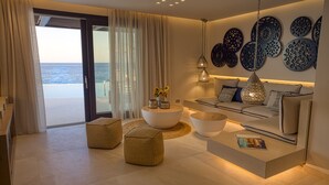 Uma sala de estar moderna com um sofá branco grande, uma mesa de centro redonda e vista para o oceano através de uma porta de vidro.