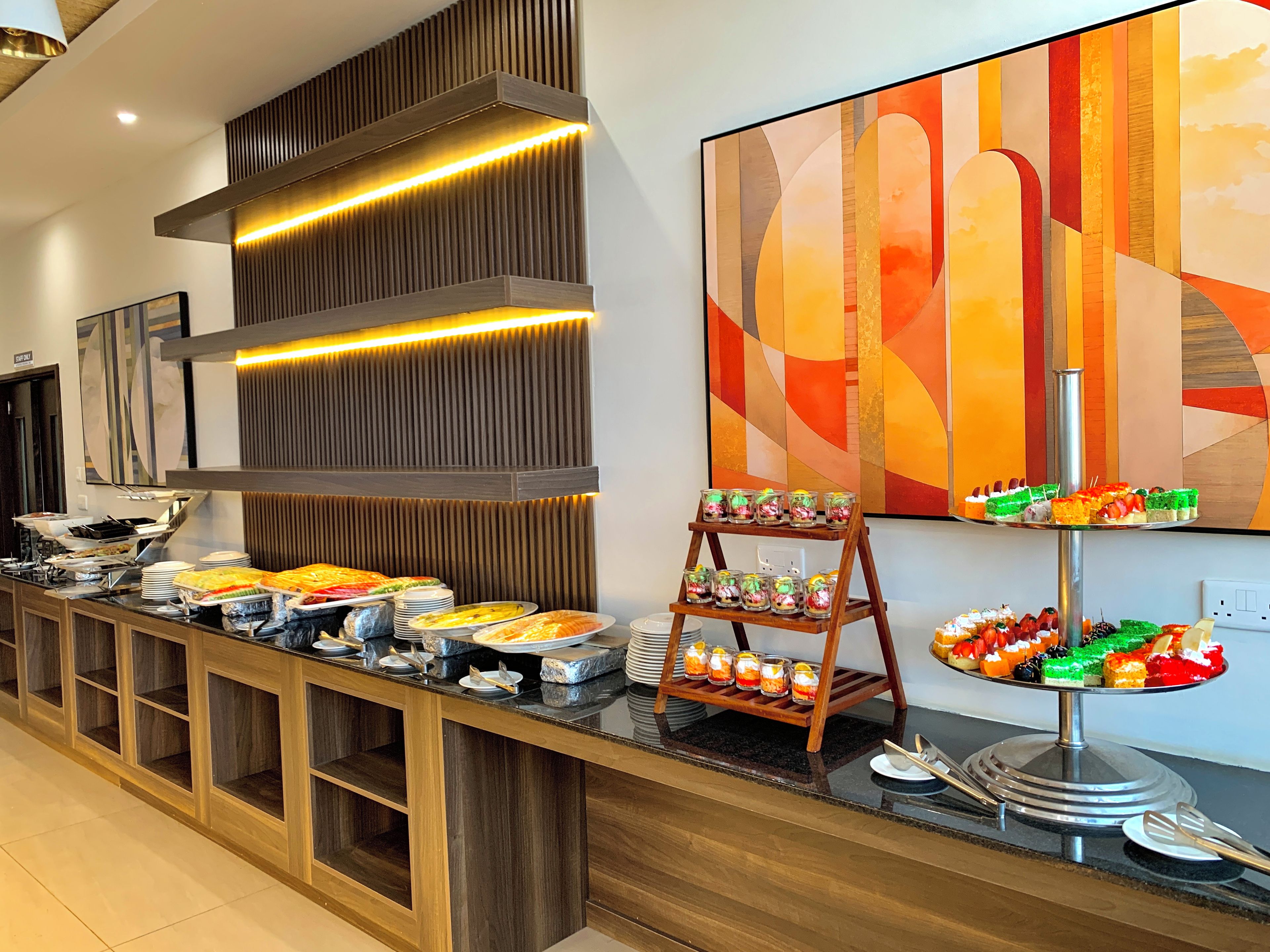 Disposição de buffet com diversos alimentos e uma pintura abstrata decorativa na parede.