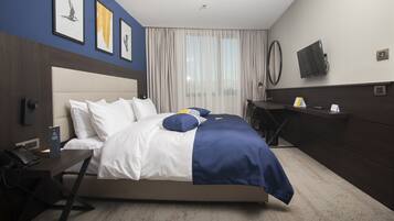 Quarto de hotel com cama, escrivaninha, telefone, televisão e janela com cortinas.