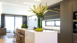 Cozinha moderna com ilha de mármore, banquetas, um vaso de flores e uma janela grande.