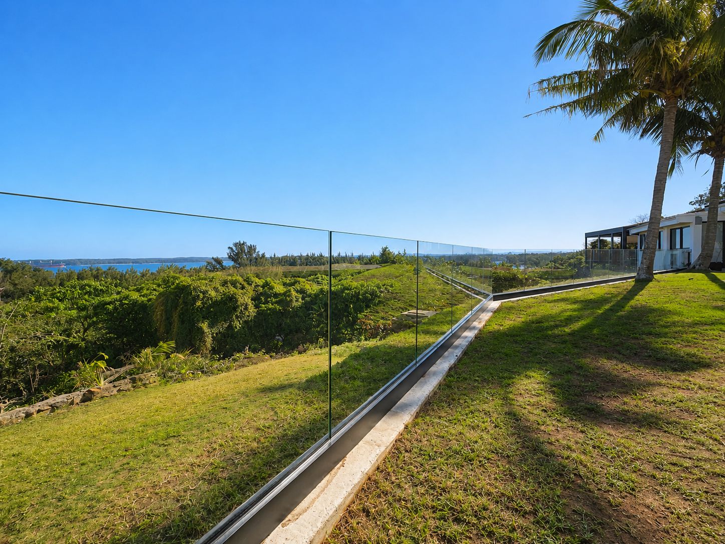 Uma casa moderna com guarda-corpo de vidro, vista para uma área gramada e um corpo d'água.