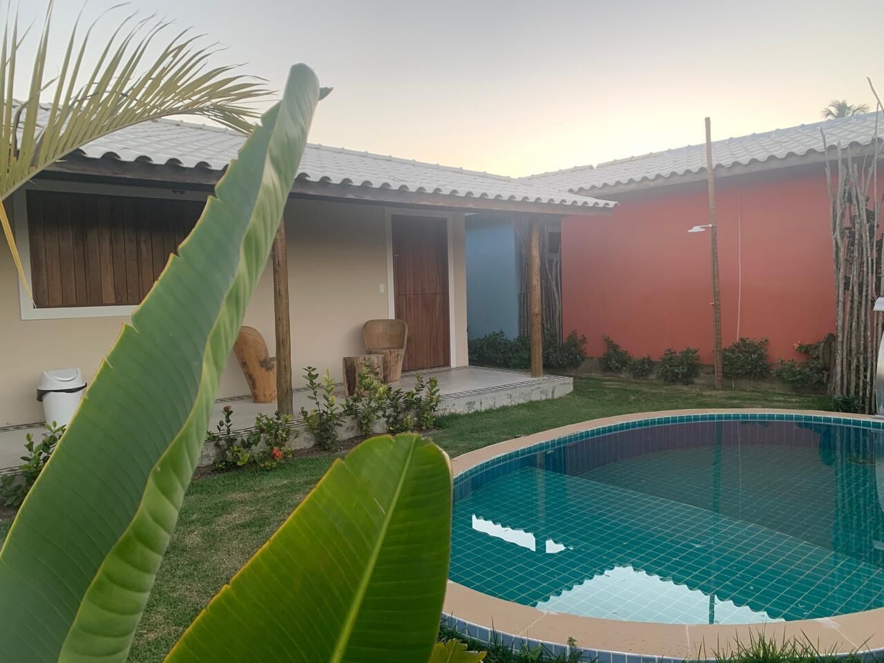 Um imóvel residencial com piscina, varanda coberta e jardim com plantas tropicais.