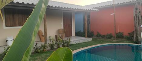 Um imóvel residencial com piscina, varanda coberta e jardim com plantas tropicais.