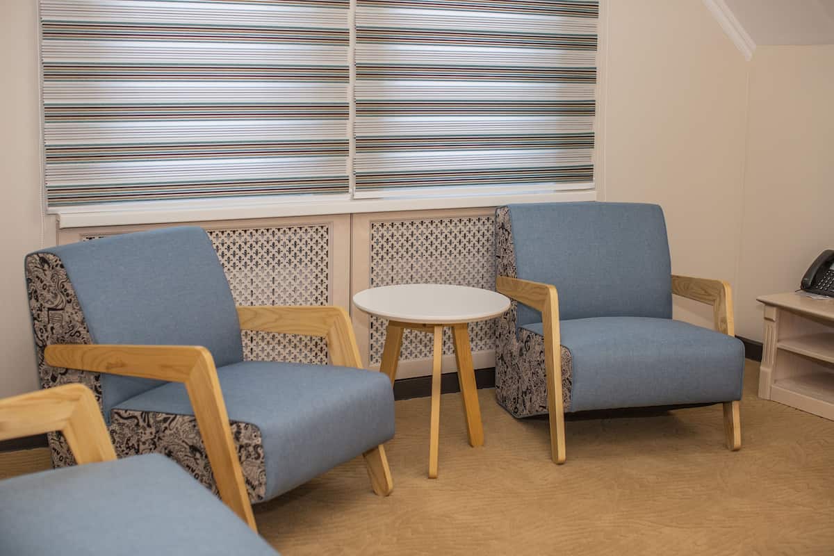 Um quarto com duas poltronas azuis, uma pequena mesa branca e uma parede estampada.
