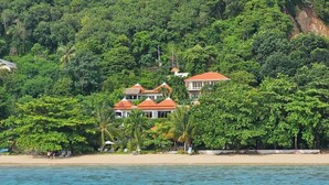 Uma propriedade costeira com vários edifícios, uma praia e uma colina arborizada.
