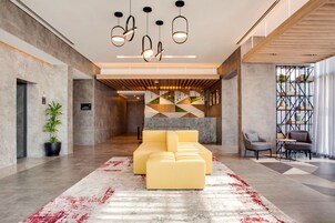Um lobby moderno com um sofá de canto, uma escada e uma área de estar com cadeiras e uma mesa.