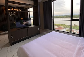 Quarto de hotel com uma cama grande, uma TV sobre um suporte de madeira e vista para um rio.