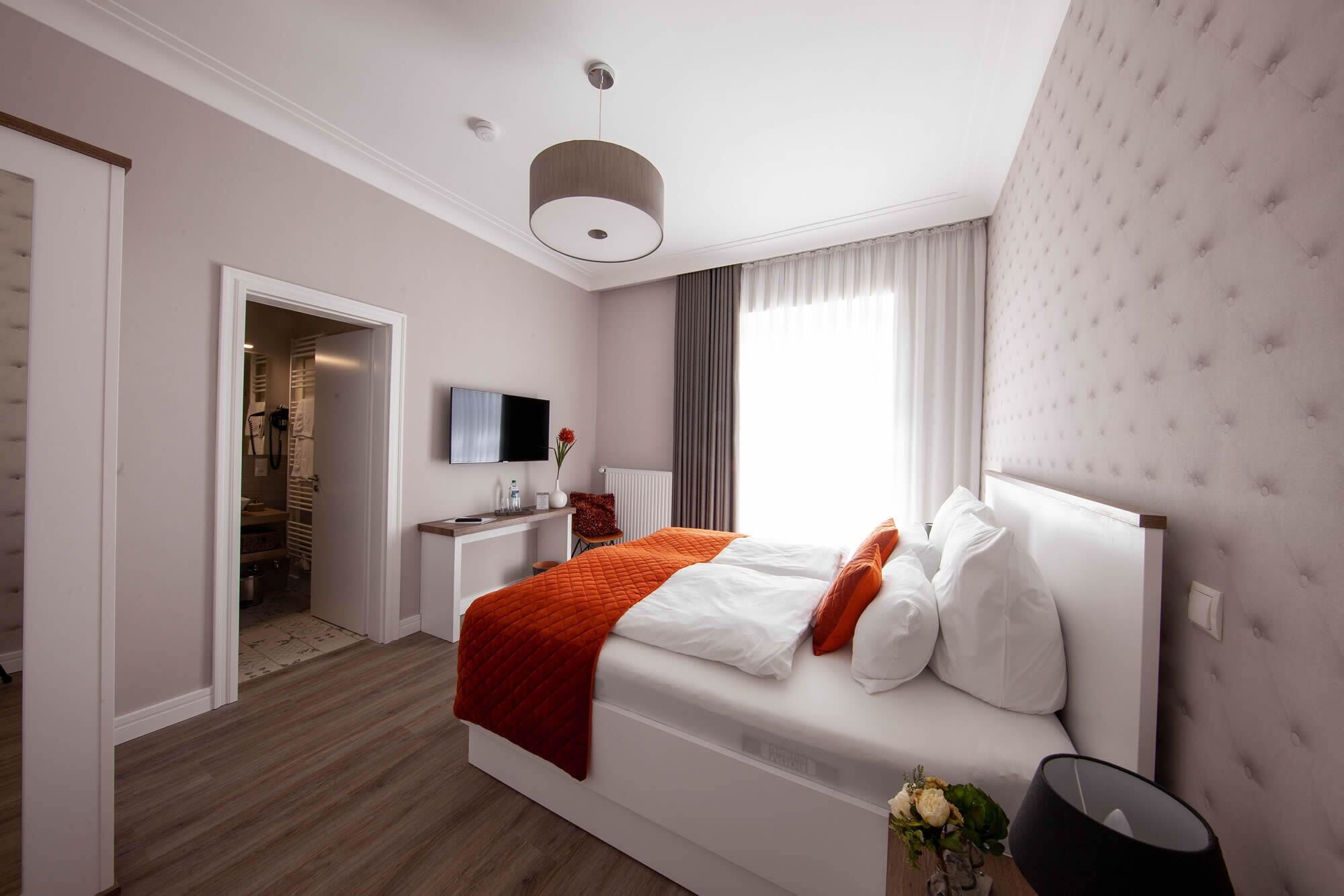 Quarto de hotel moderno com cama, televisão, mesa de cabeceira e vista para o exterior.
