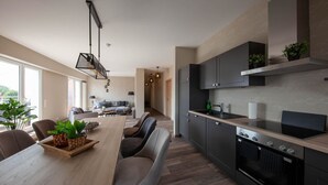 Uma cozinha moderna com armários escuros, forno embutido e uma área de refeições com mesa e cadeiras de madeira.