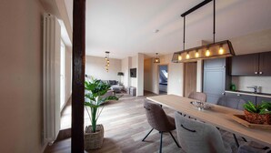 Cozinha moderna com área de refeições, apresentando uma mesa de madeira comprida, duas cadeiras e iluminação pendente.