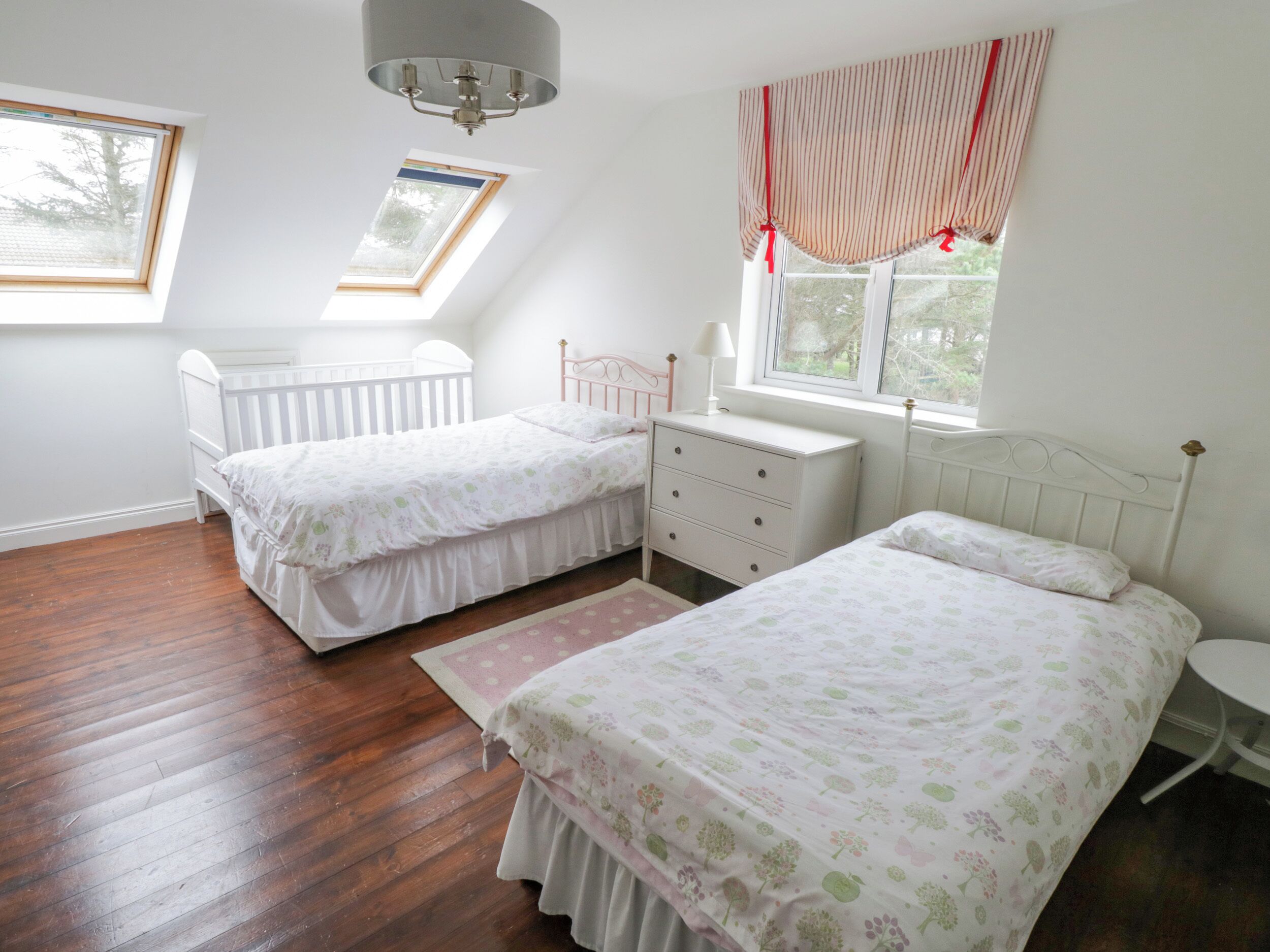 Quarto com duas camas, penteadeira, janela com cortinas, claraboia e luz de teto.