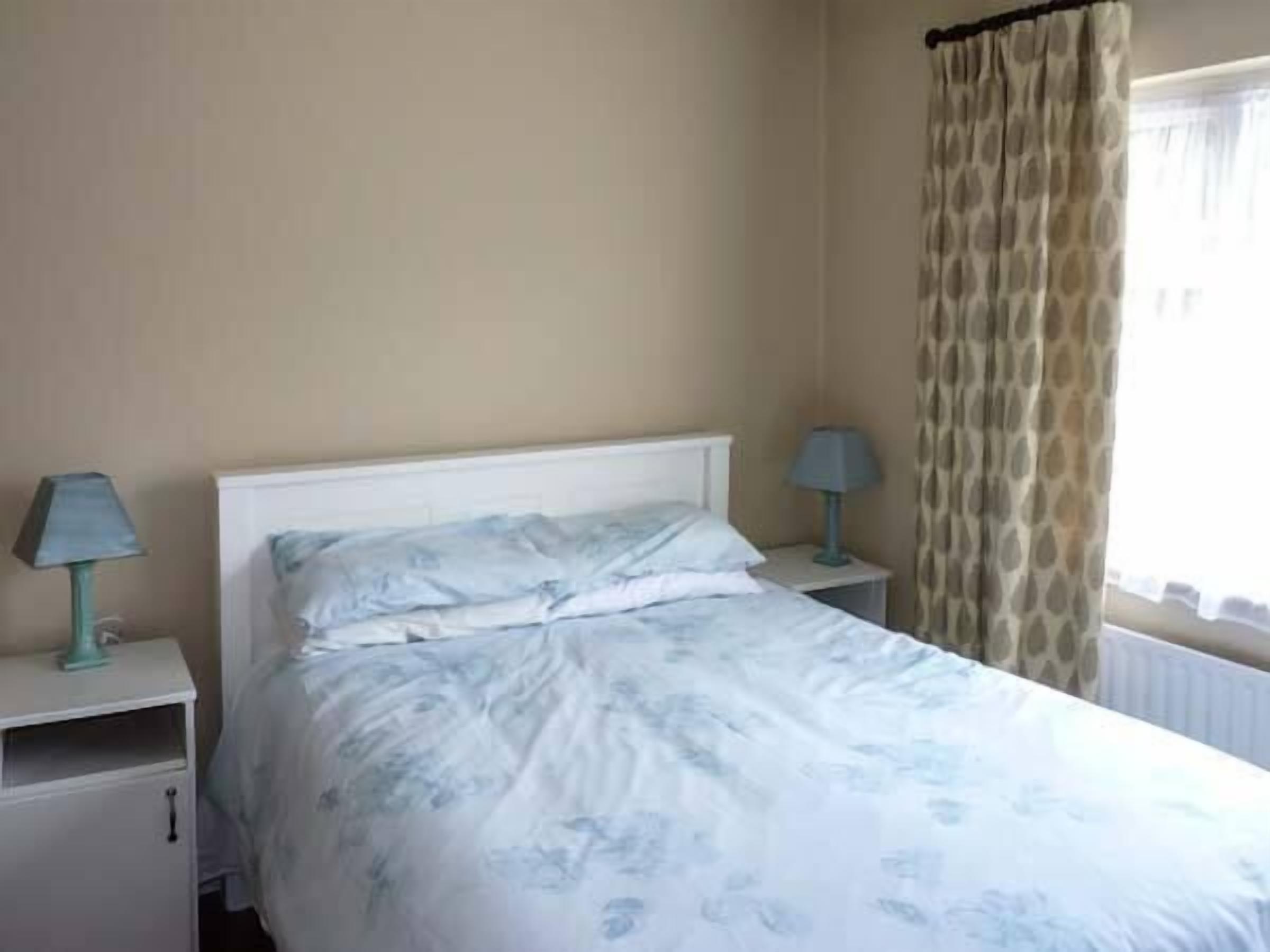Quarto com uma cama de solteiro, duas mesas de cabeceira e uma janela com cortinas.