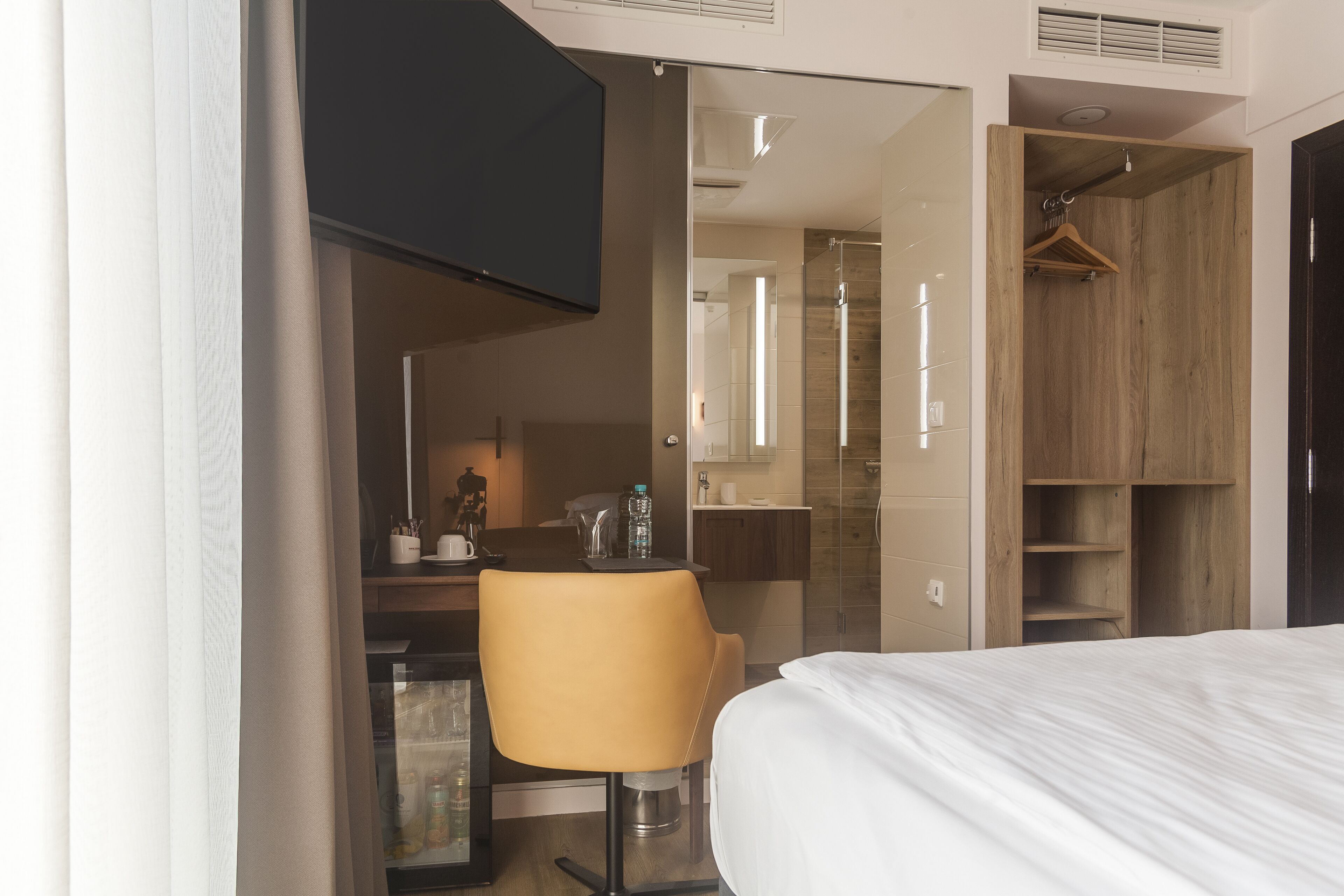 Quarto de hotel com cama, secretária com cadeira, guarda-roupa e televisão.
