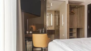 Quarto de hotel com cama, secretária com cadeira, guarda-roupa e televisão.