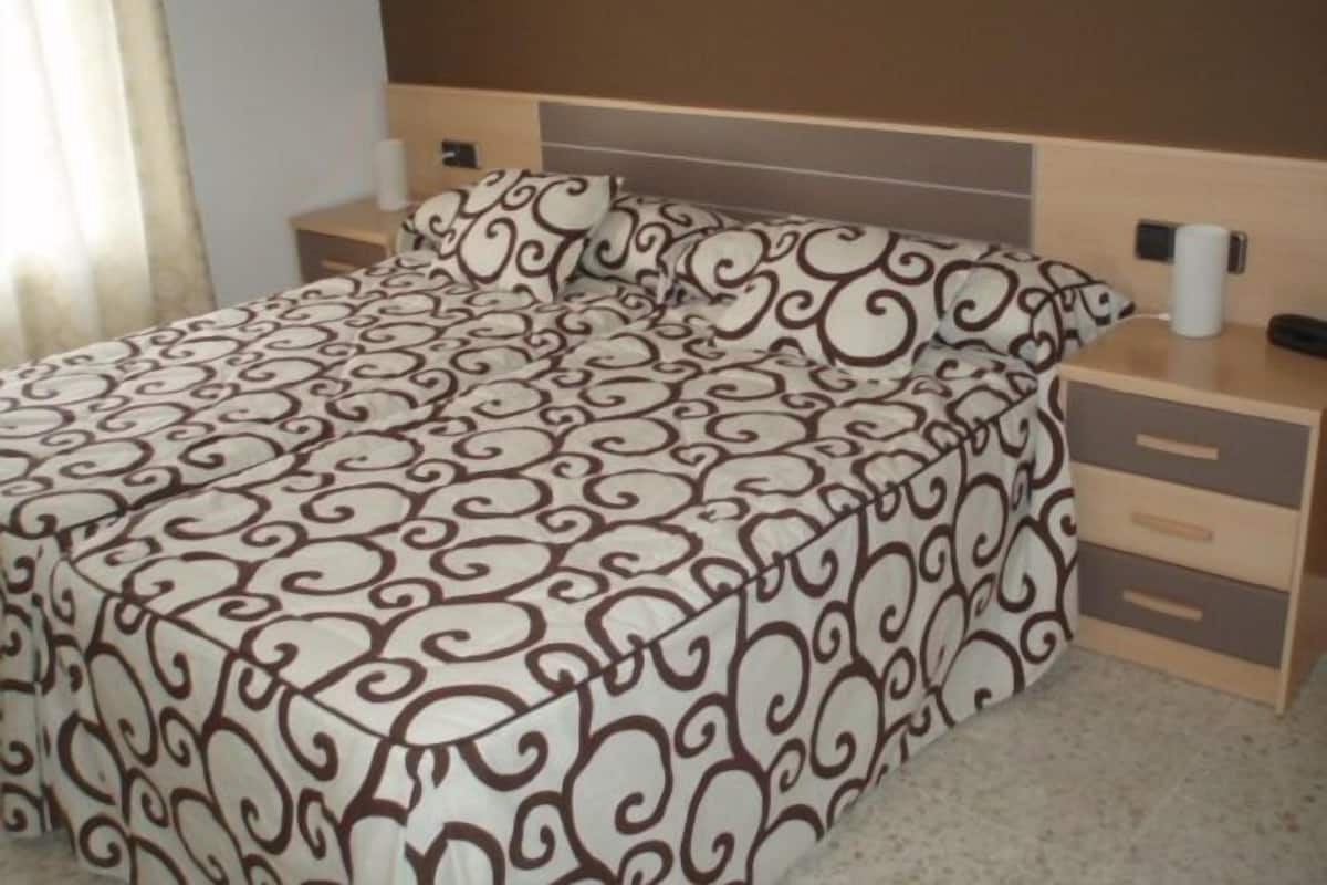 Quarto de hotel com uma cama, mesa de cabeceira e gaveteiro.