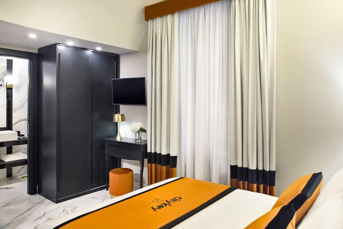 Quarto de hotel moderno com cama, escrivaninha, televisão e guarda-roupa.