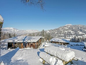 Uma cabana coberta de neve com uma vista desobstruída de montanhas nevadas ao fundo.