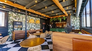 Interior de restaurante com piso xadrez, mesas e cadeiras de madeira, área de bar e papel de parede tropical.