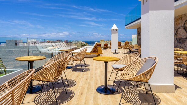 Terraço no telhado com cadeiras e mesas de vime, com vista para a cidade e o mar.