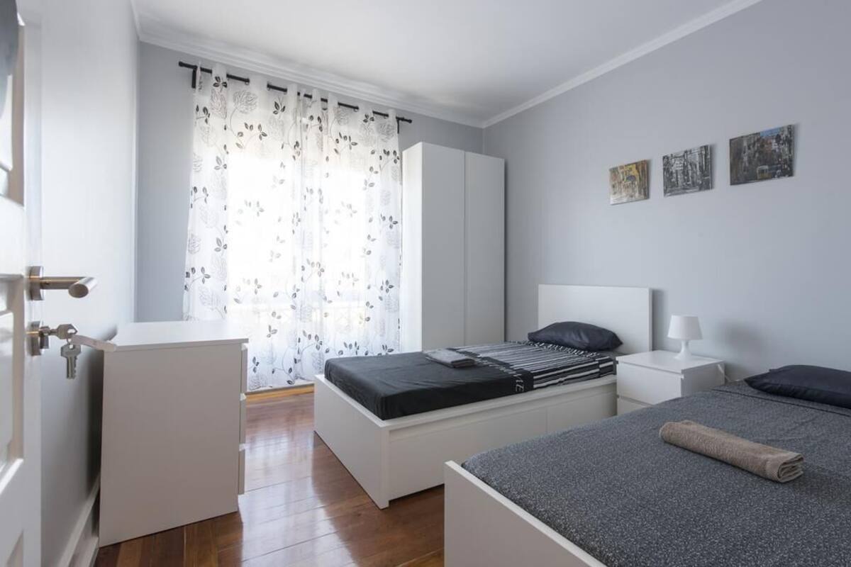 Quarto com cama, mesas de cabeceira, guarda-roupa e janela com cortinas.