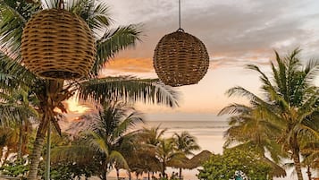 Cena de praia com palmeiras, uma estrutura de telhado de palha e cadeiras de praia.