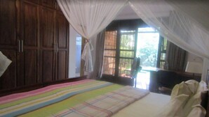 Quarto com cama grande, guarda-roupa de madeira e janela com vista para o verde.