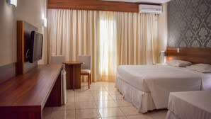 Quarto de hotel com cama, escrivaninha, cadeira e televisão.