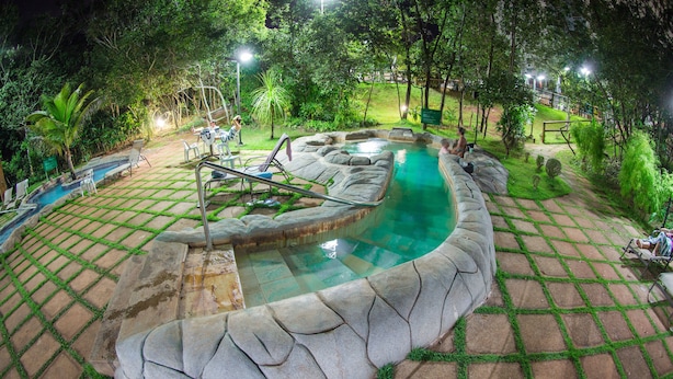 Uma piscina com um design de pedra original, rodeada por um espaço pavimentado com áreas de relvado.