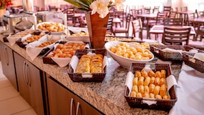 Buffet com diversos alimentos, incluindo pães e doces, dispostos sobre uma bancada de mármore.