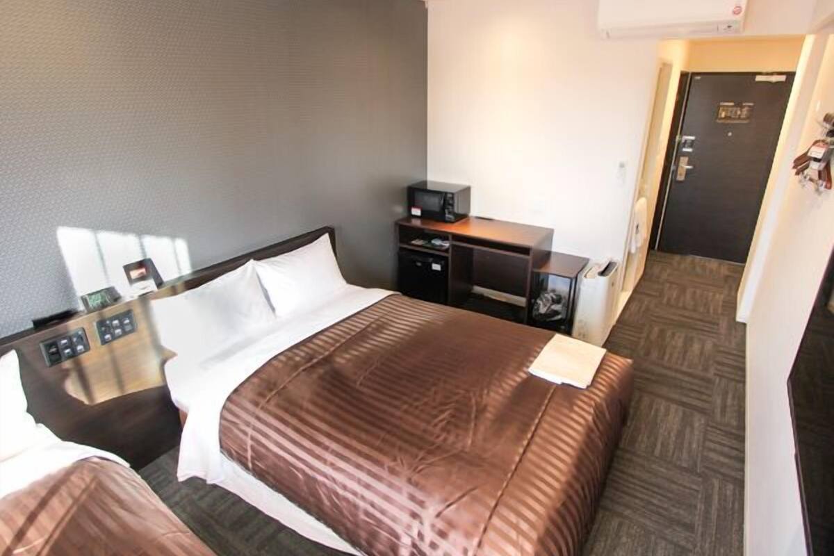 Quarto de hotel com cama, mesas de cabeceira, escrivaninha, cadeira, guarda-roupa e ar condicionado.