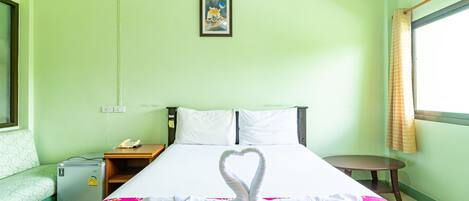 Quarto de hotel com cama, pequena escrivaninha, frigorífico e janela com cortinas.