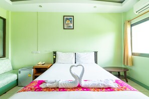 Quarto de hotel com cama, pequena escrivaninha, frigorífico e janela com cortinas.