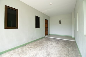 Um corredor com piso claro, uma porta de madeira no final e duas janelas com molduras castanhas.