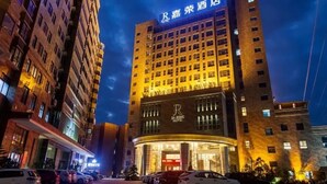 Edifício de hotel com sinalização iluminada, área de estacionamento com carros e edifícios vizinhos.