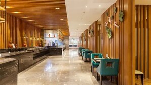 Um saguão de hotel com balcão de recepção, área de bar e assentos com cadeiras verdes.